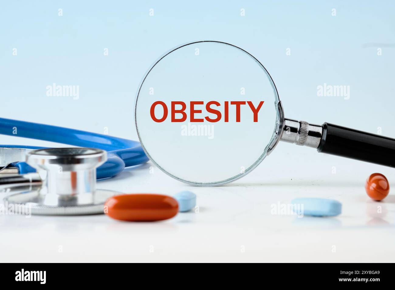 OBESITY word written through a magnifying glass on a blue background ...