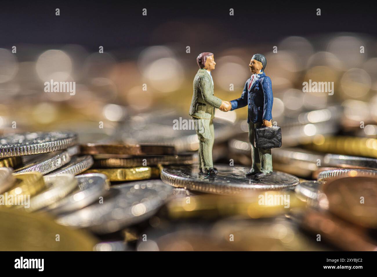 Small figures of two men shaking hands on a pile of coins Stock Photo ...