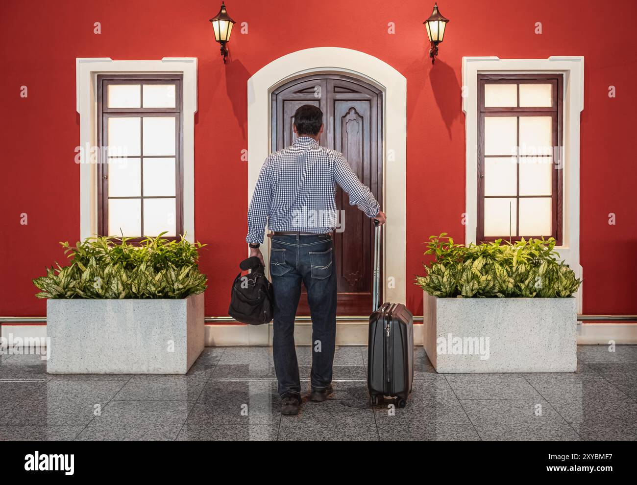 Man with suitcase standing in front of closed door in hotel. Young man ...