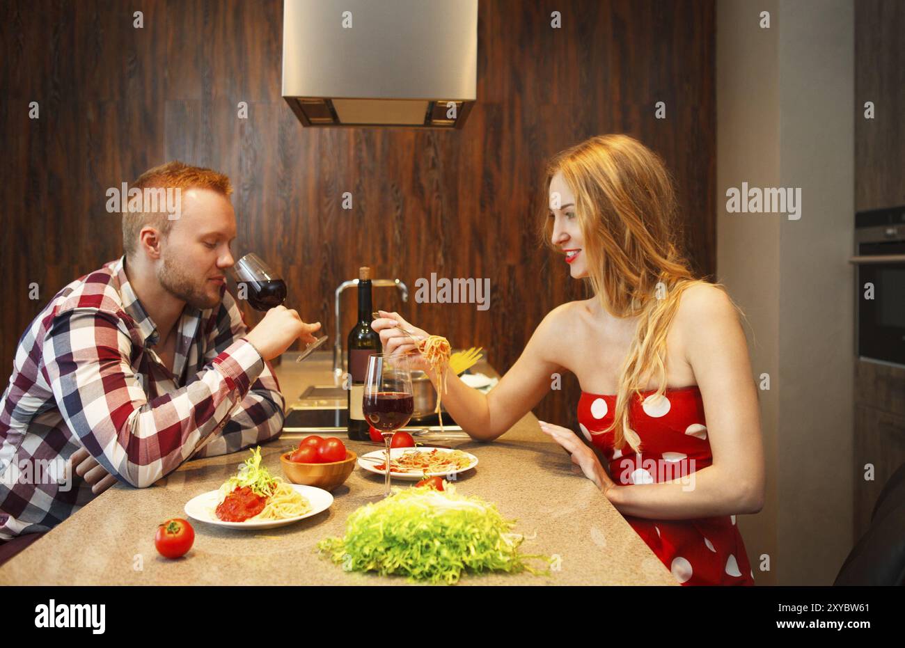 Happy woman eating pasts while man tasting red wine in a kitchen ...