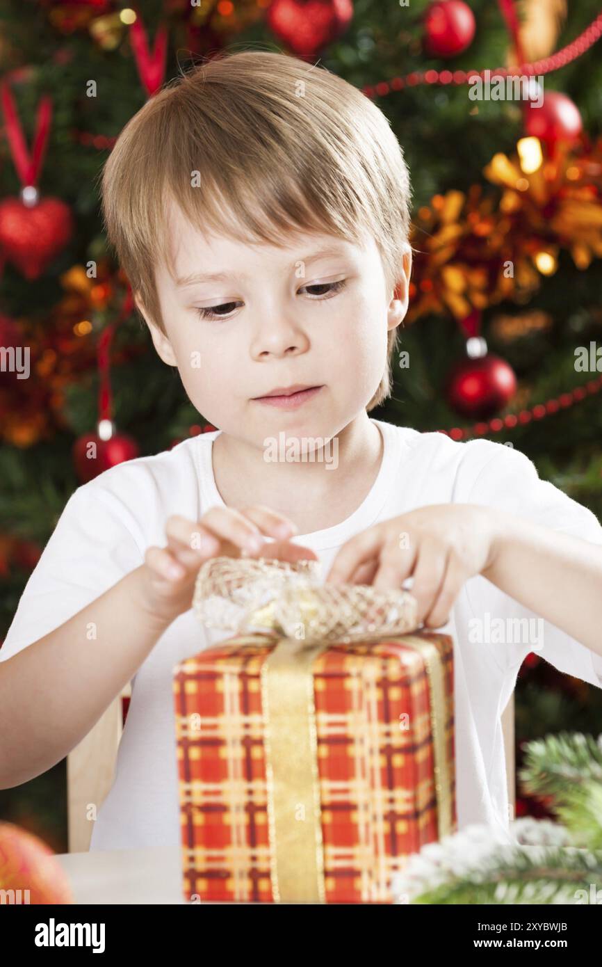 Surprised boy opening present against Christmas tree with decorations ...