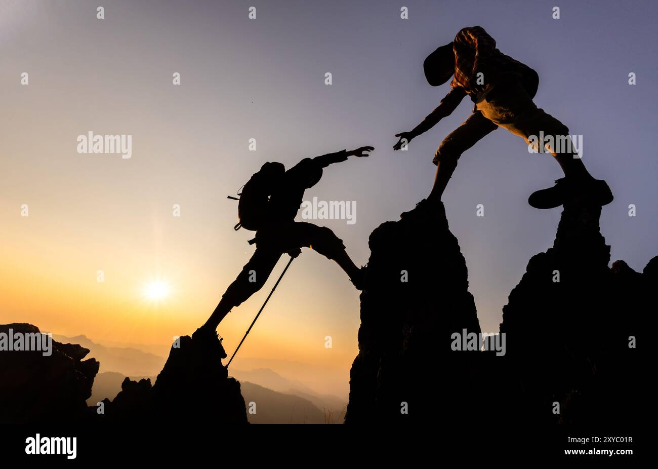 Silhouette of hiker helping each other hike up a mountain at sunset ...