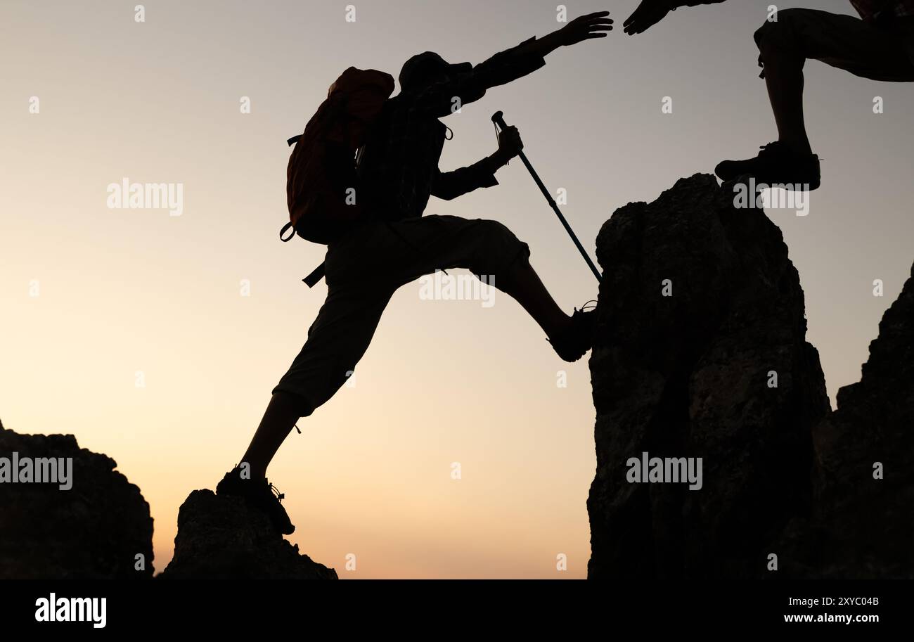 Silhouette of hiker helping each other hike up a mountain at sunset ...