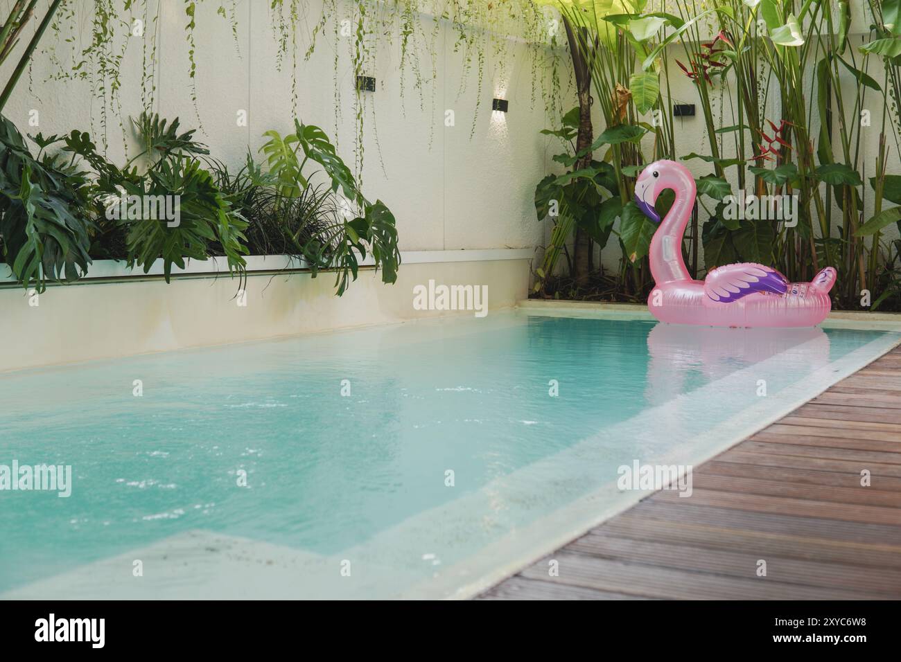 A pink inflatable flamingo floats in a pool. The pool is in a backyard ...