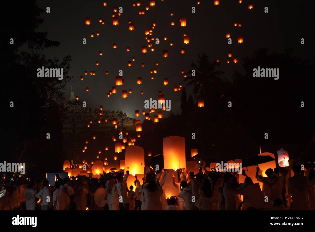 A group of people are holding lit lanterns and flying them in the air during Vesak Day ceremony ...