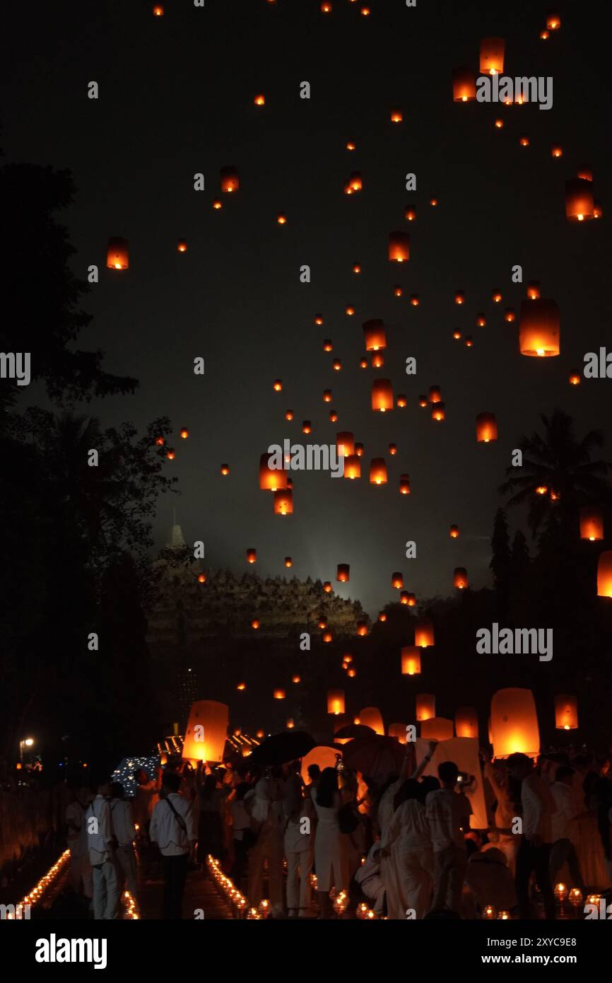 Vertical oriented picture of people are holding lit lanterns and flying them in the air during ...