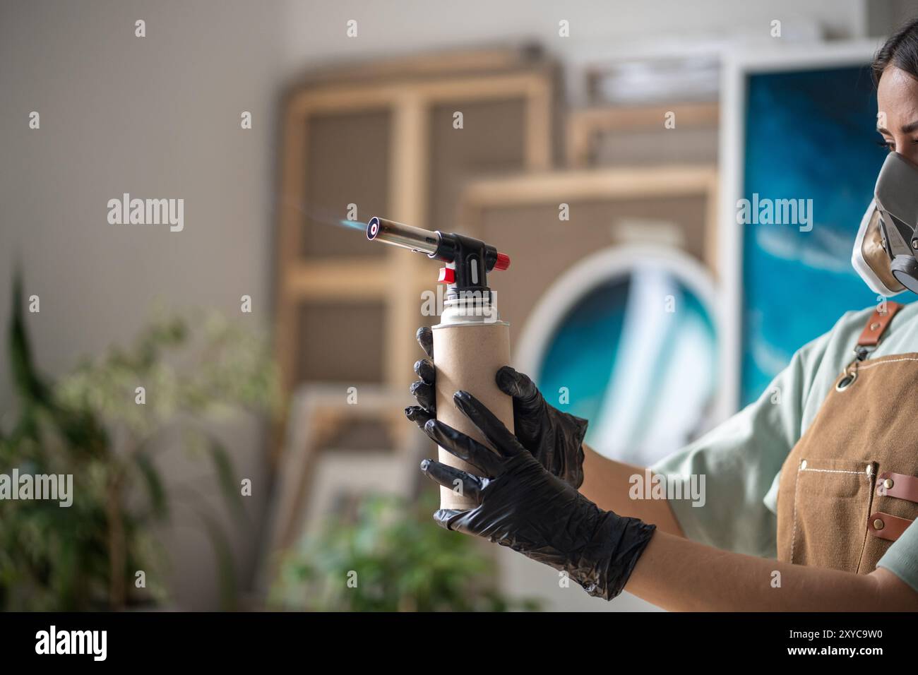 Woman with respirator ignites blowtorch, adjusts flame in artist ...