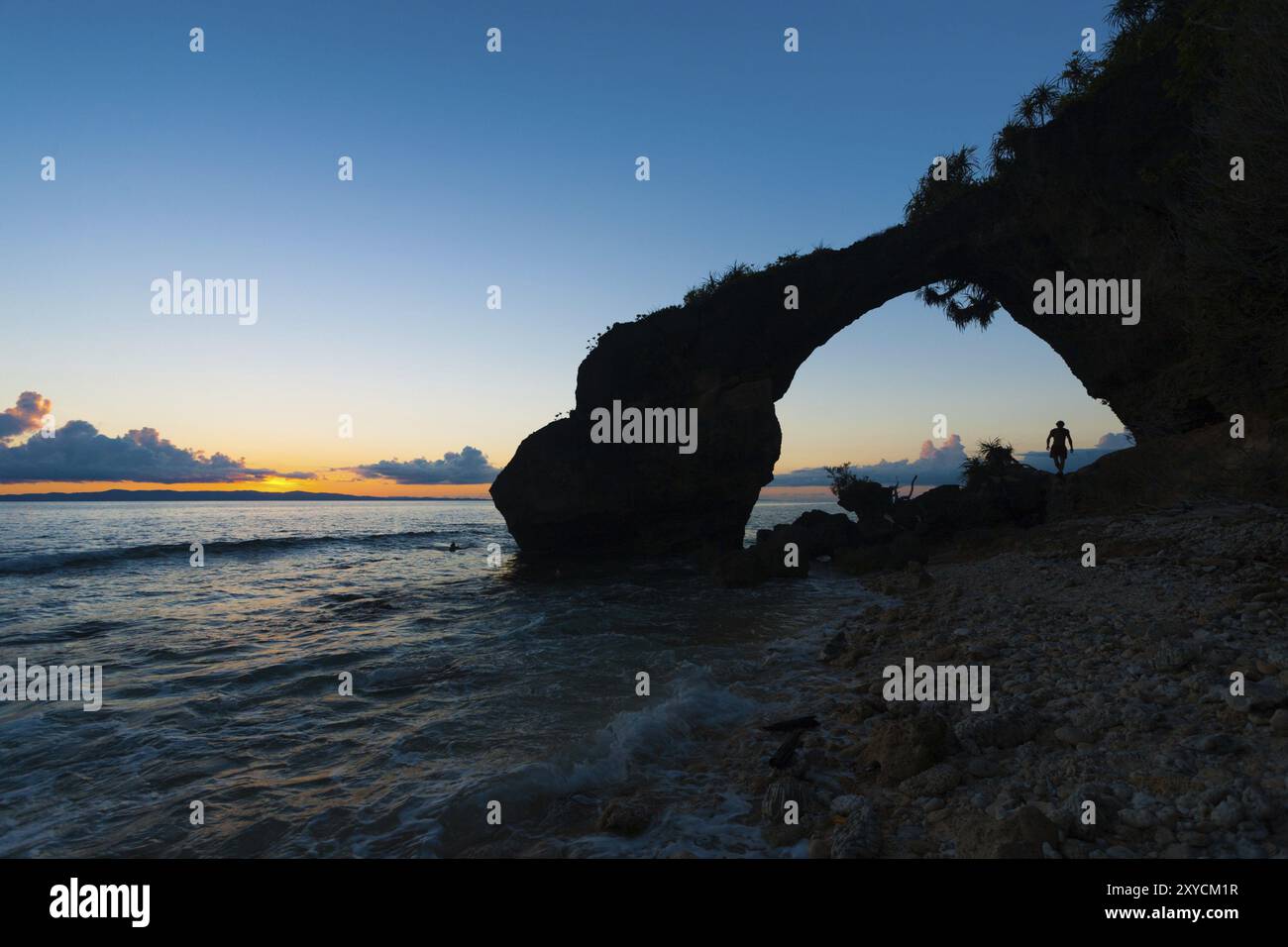 The sunset glows orange below the horizon behind the natural bridge and ...