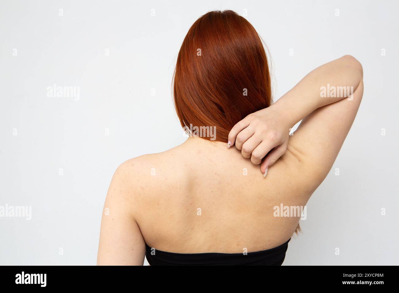 Young woman is scratching her back with her hand on a white background ...