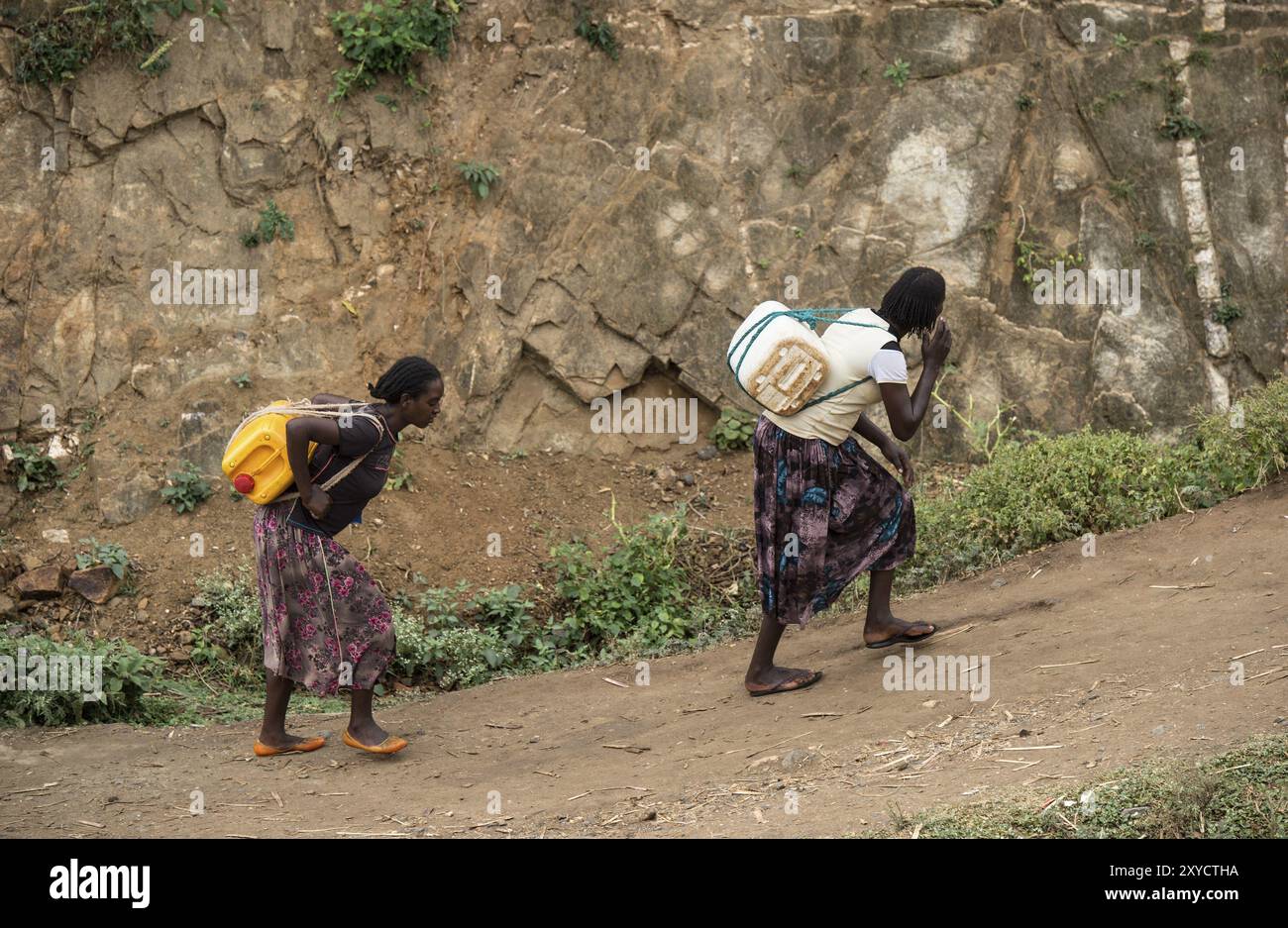Two woman carry heavy water canisters on their backs from the water ...