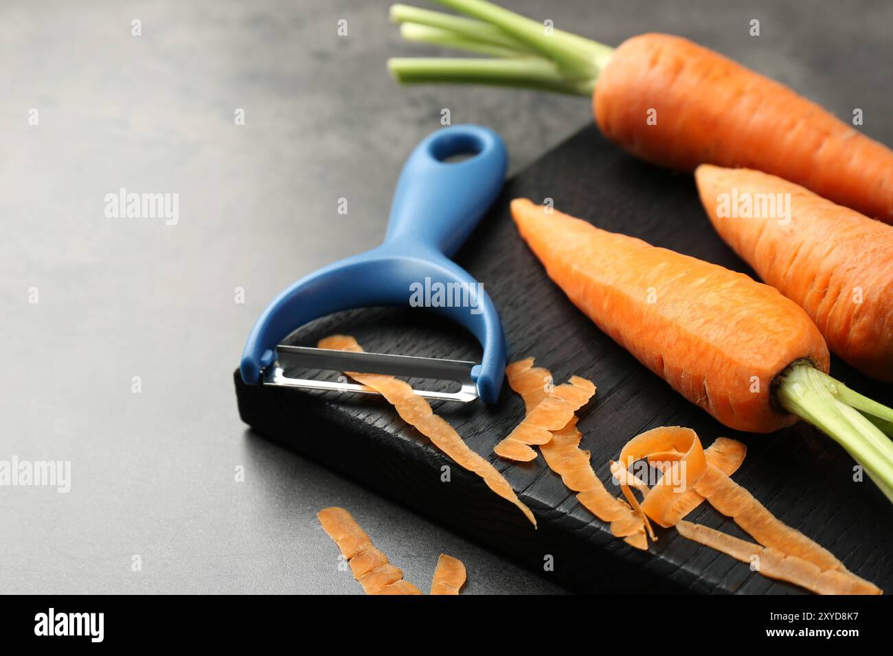 Fresh carrots, vegetable peeler and peels on gray textured table ...