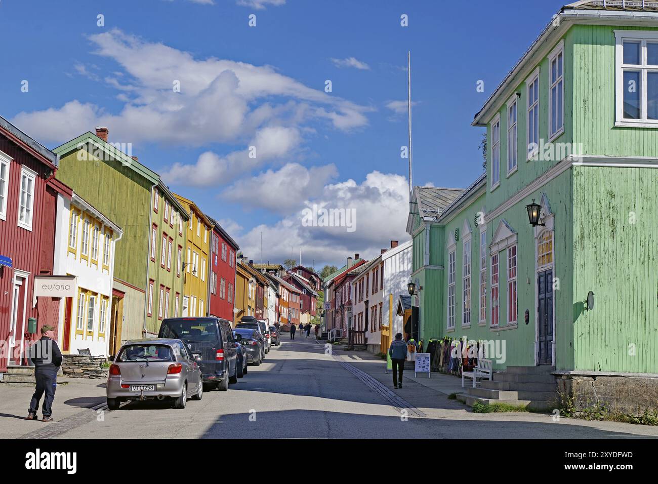 Lively city street with colourful wooden buildings, parked cars and a ...