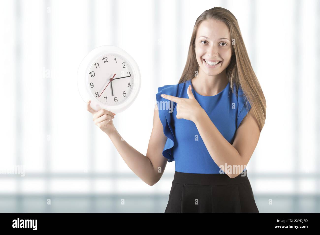 Young woman smiling and pointing at a clock. Isolated in white Stock ...