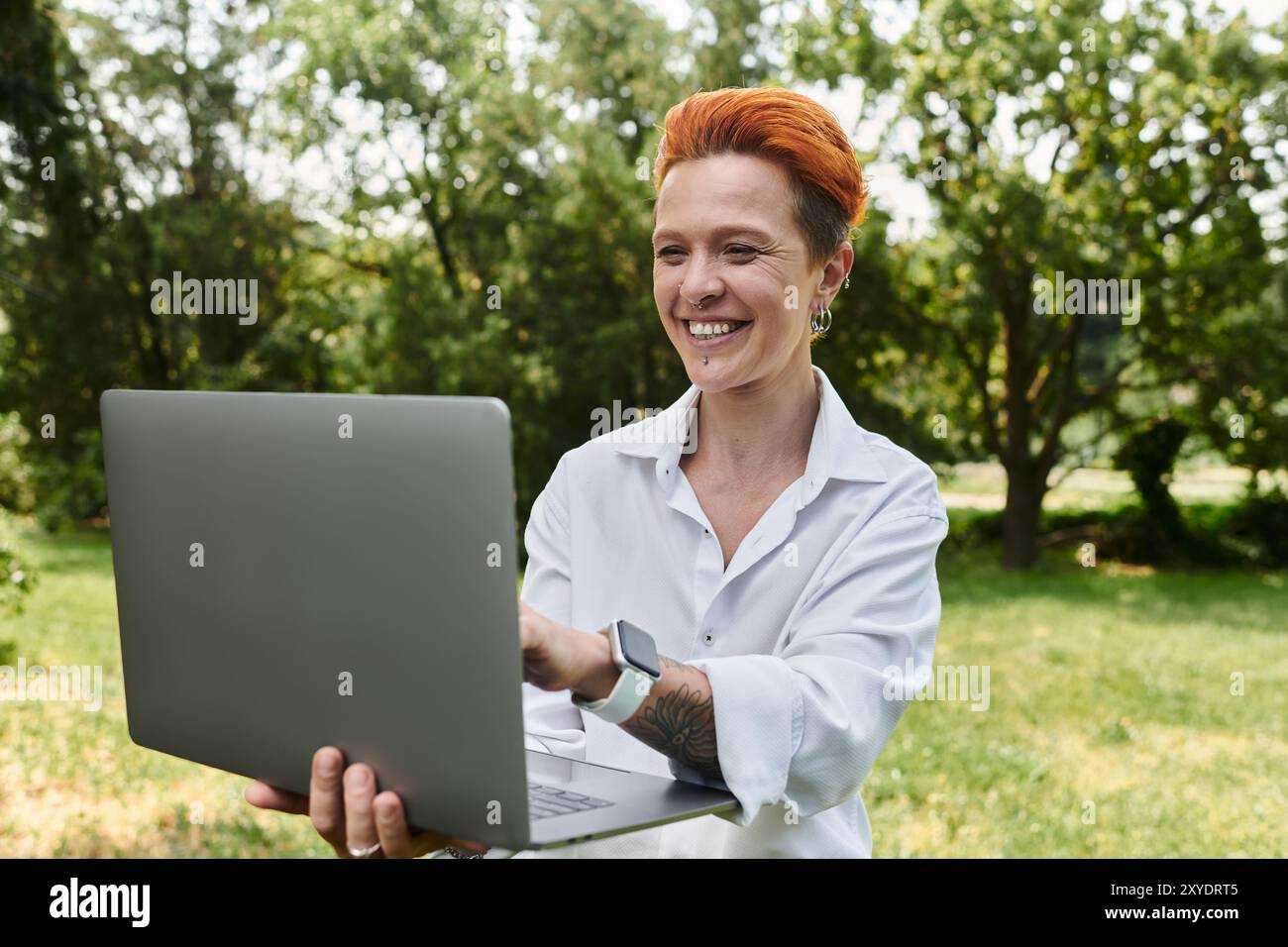 A teacher with short, bright red hair smiles as she works on her laptop ...