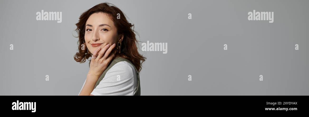 Asian woman in stylish vest poses against grey backdrop, hand resting ...