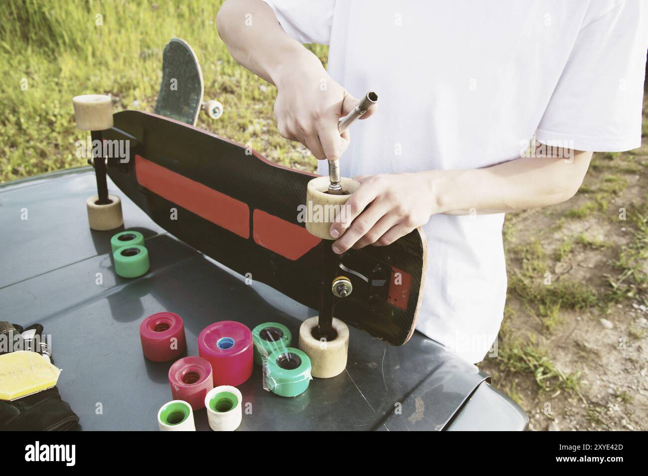 A close-up of a young guy changes his wheels on his longboard and ...