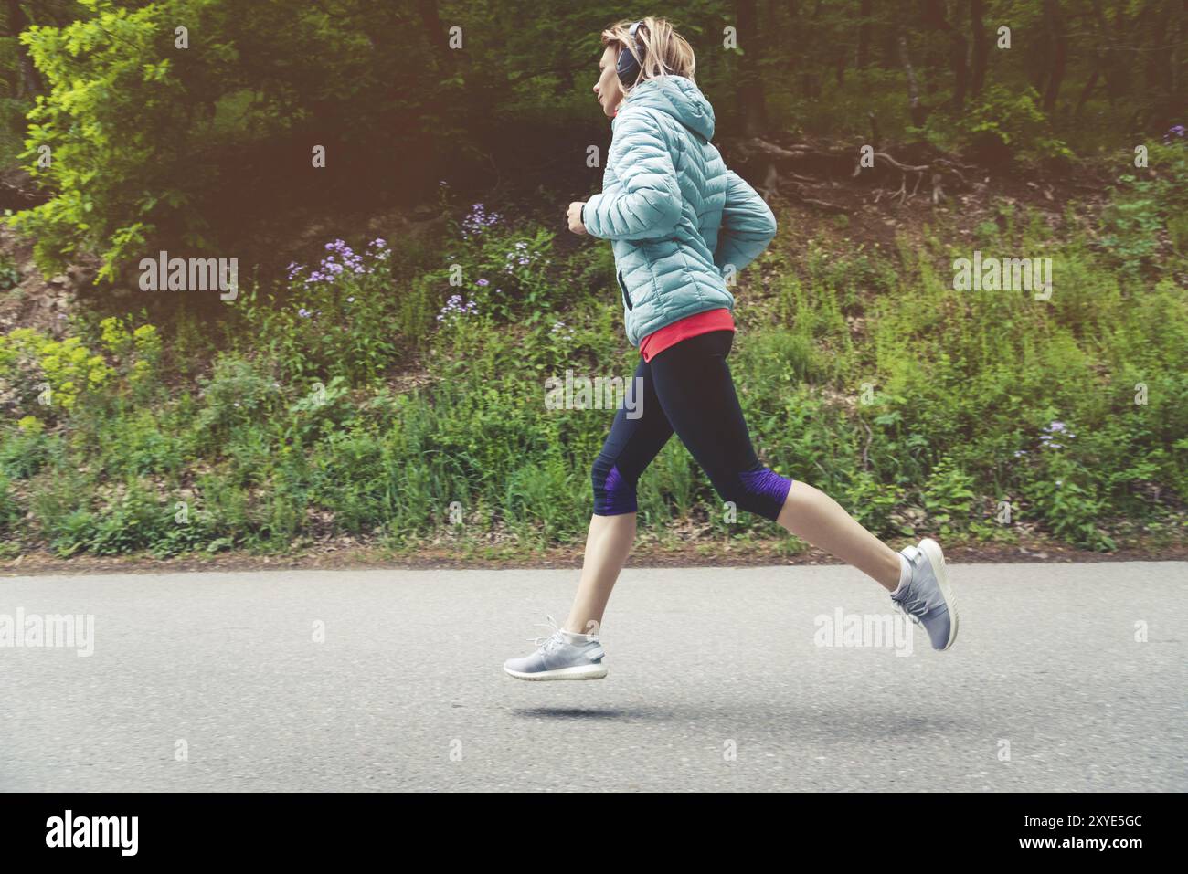 A young blonde woman running is practicing outdoors in a city mountain ...