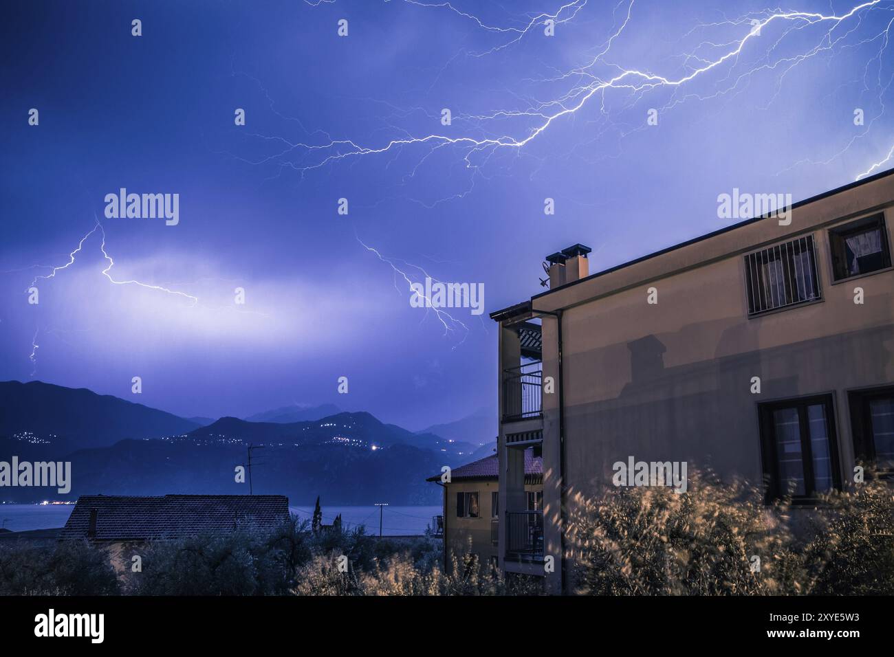 Lightning on the cloudy sky, mountains and lake, building in foreground ...
