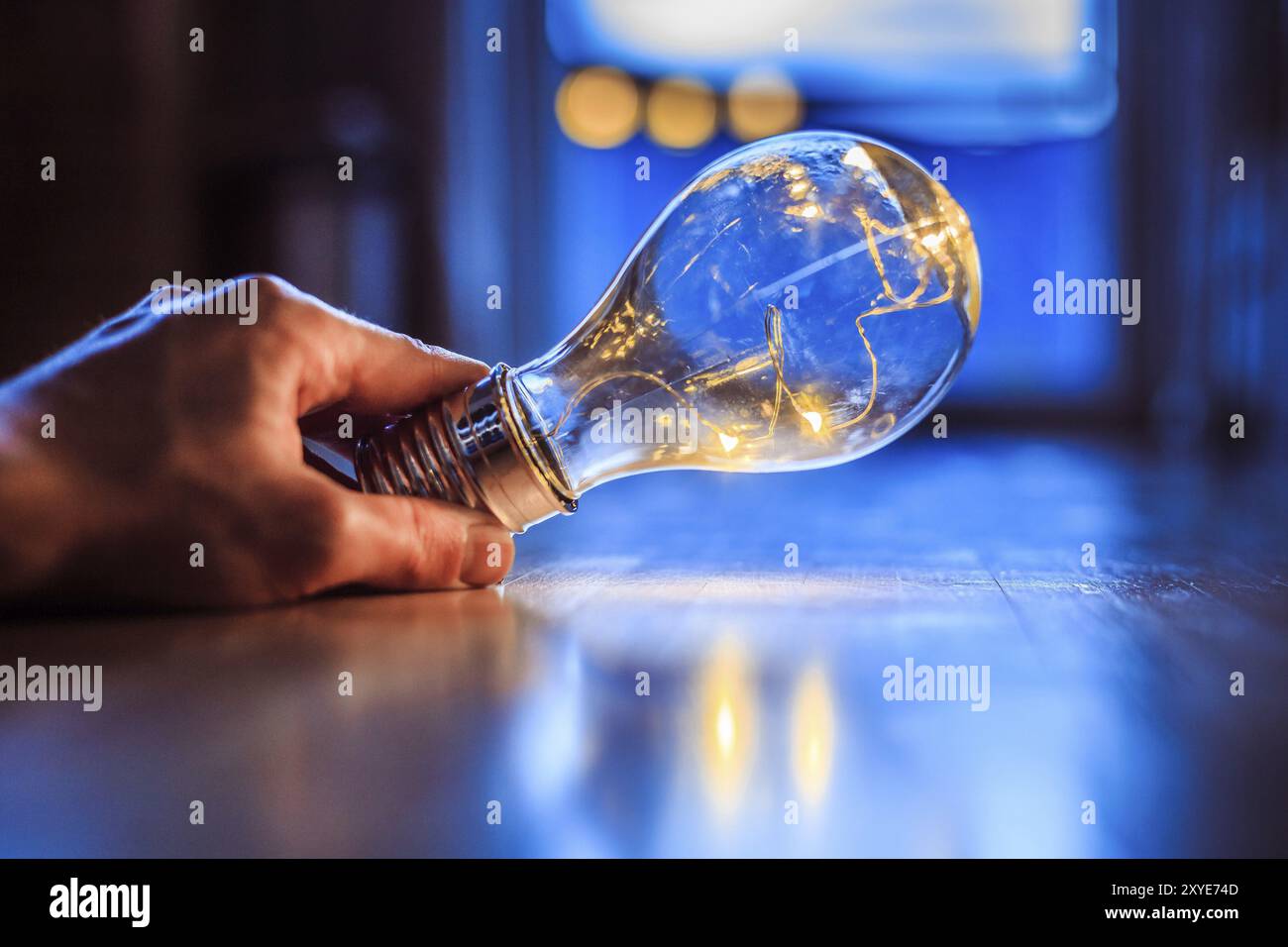Hands are holding a LED lightbulb over the wooden floor. Symbol for ...