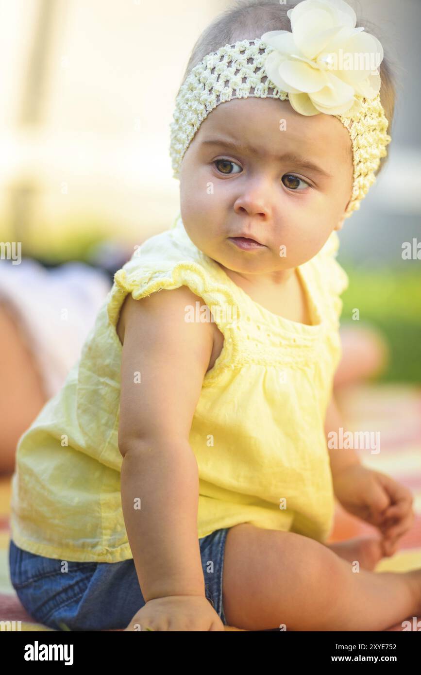 Cute baby girl in yellow band and dress sits in sunny backyard. 8 ...