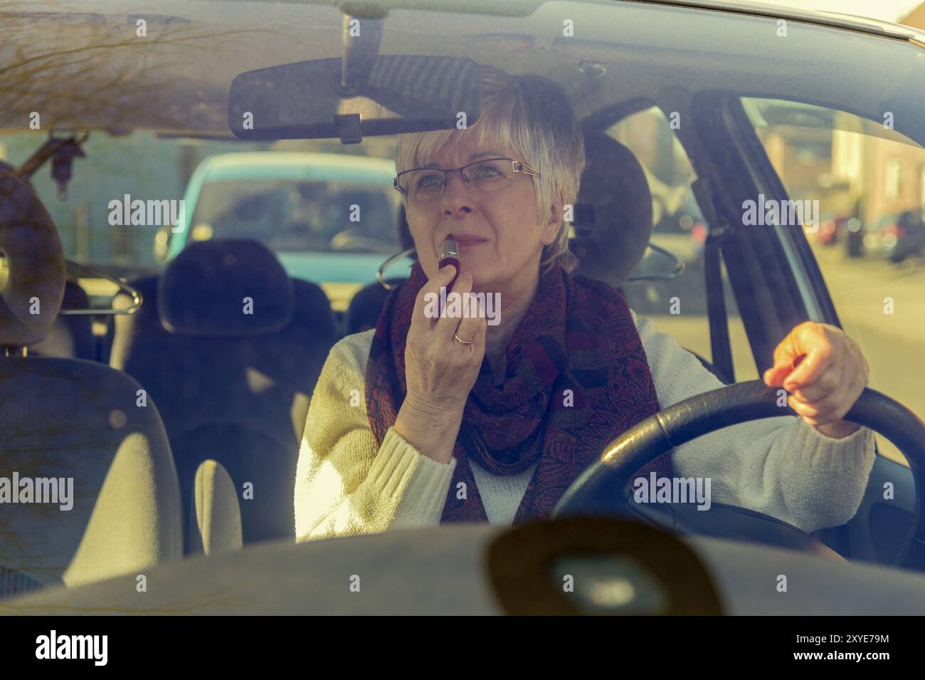 Elderly lady sits in her car, looks in the rear-view mirror and touches ...