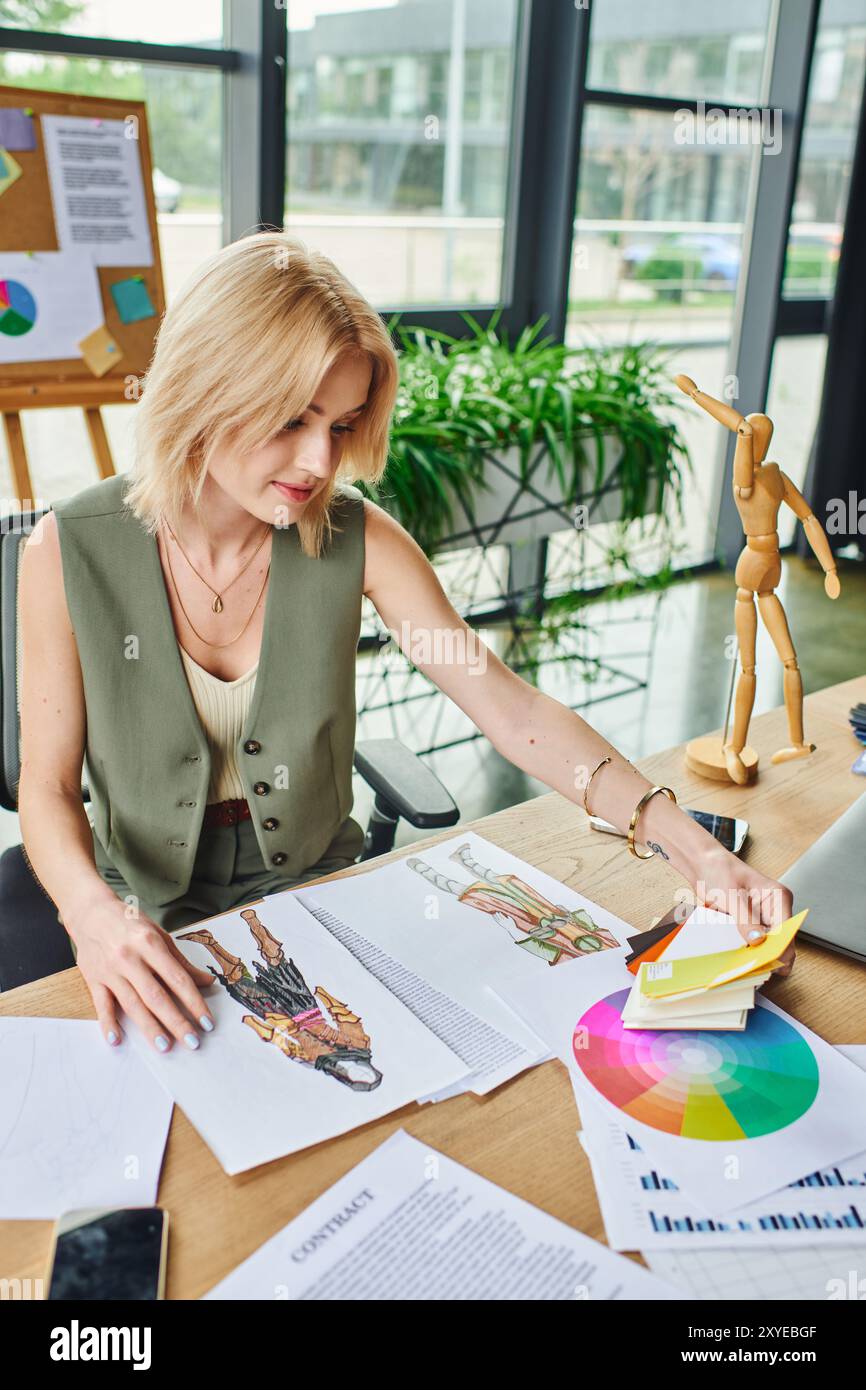 A blonde woman in a green vest and white top, sitting at her desk ...