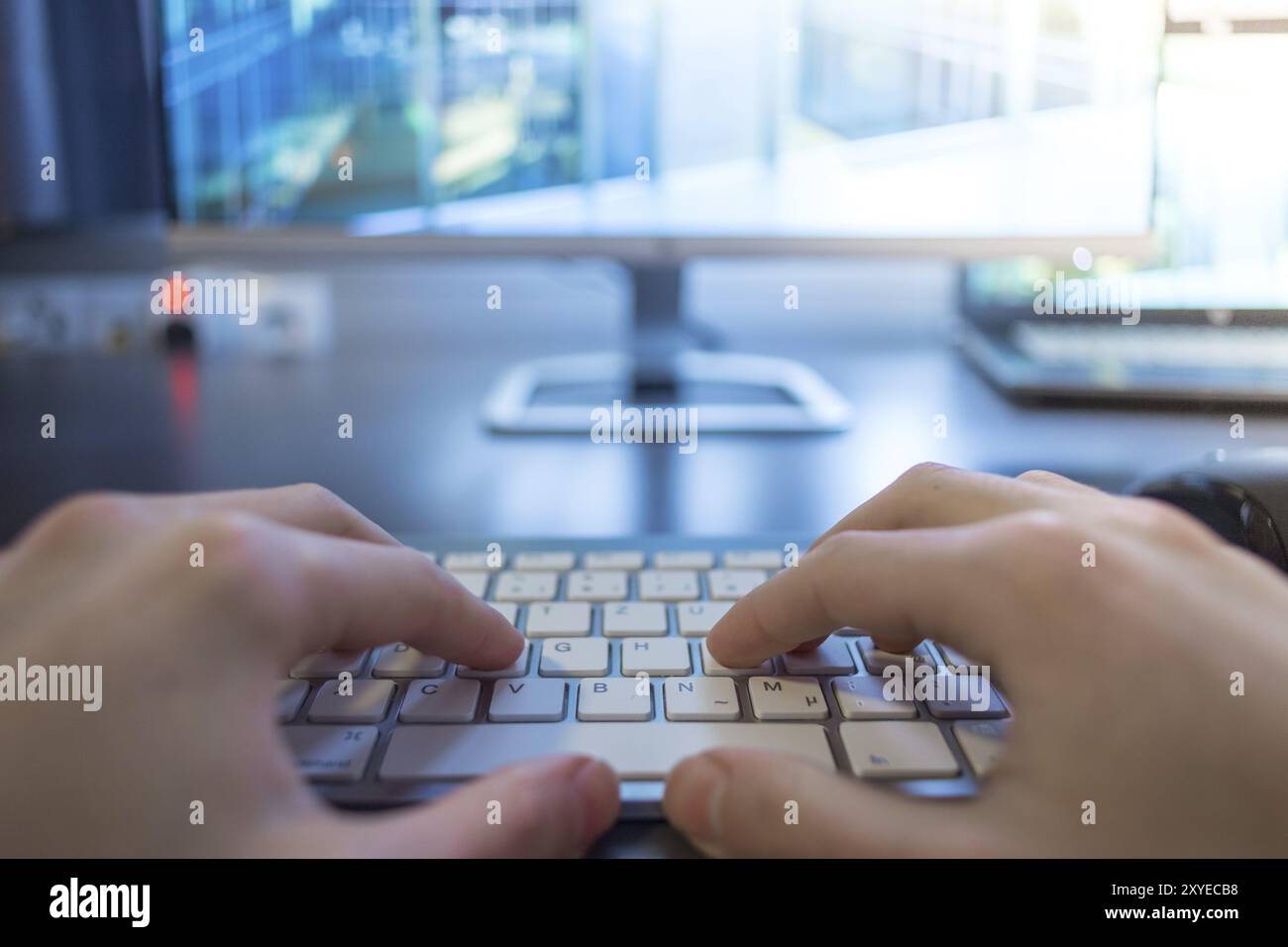 Hands are typing on a white keyboard, screen in the blurry background ...