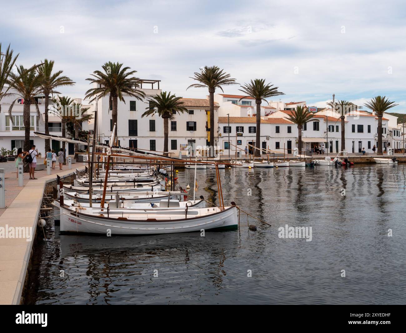 Visitors stroll along the waterfront promenade in Fornells, Menorca ...