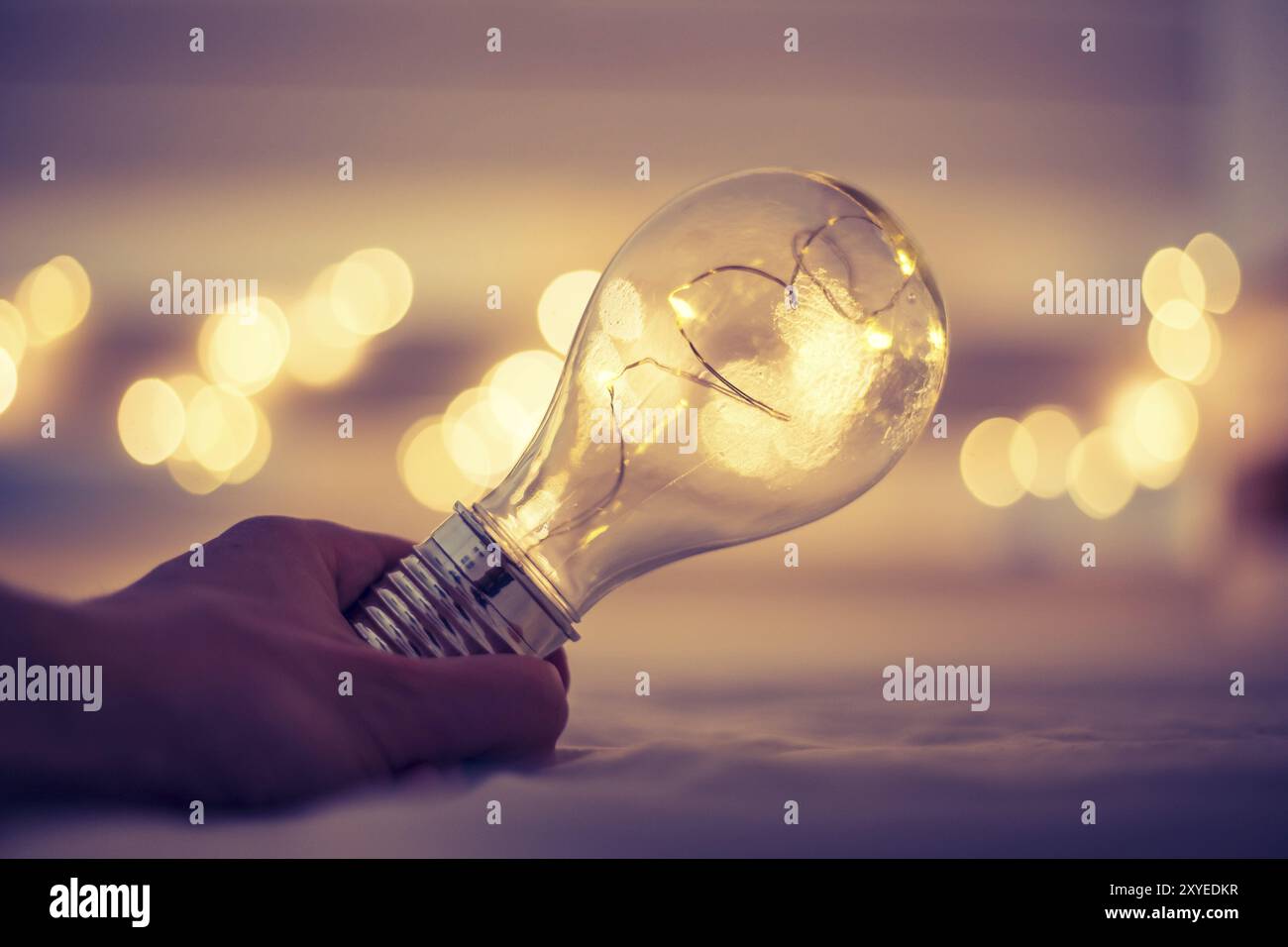 LED light bulb is lying in the bed, hands touching. Symbol for ideas ...