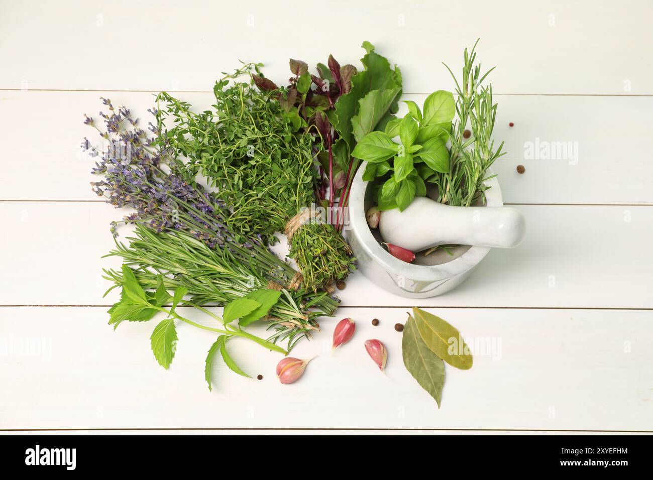 Different aromatic herbs, garlic, mortar and pestle on white wooden ...