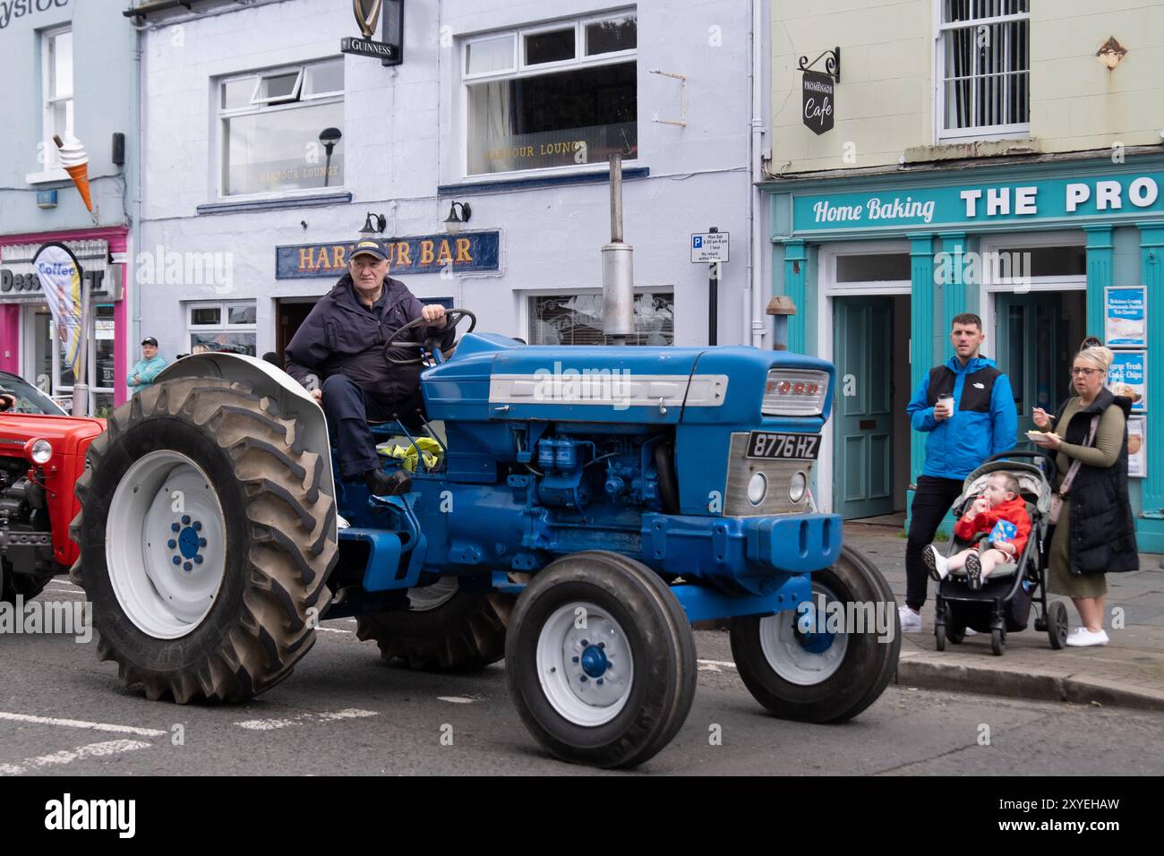 Older man wearing baseball cap driving vintage blue Ford tractor ...