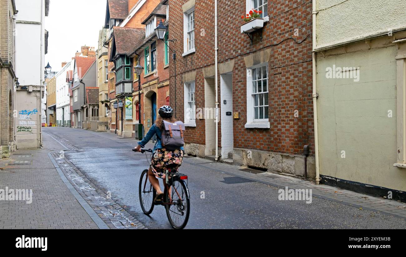 Rear back view behind of young woman cyclist riding a bike near The Story Museum on Pembroke ...