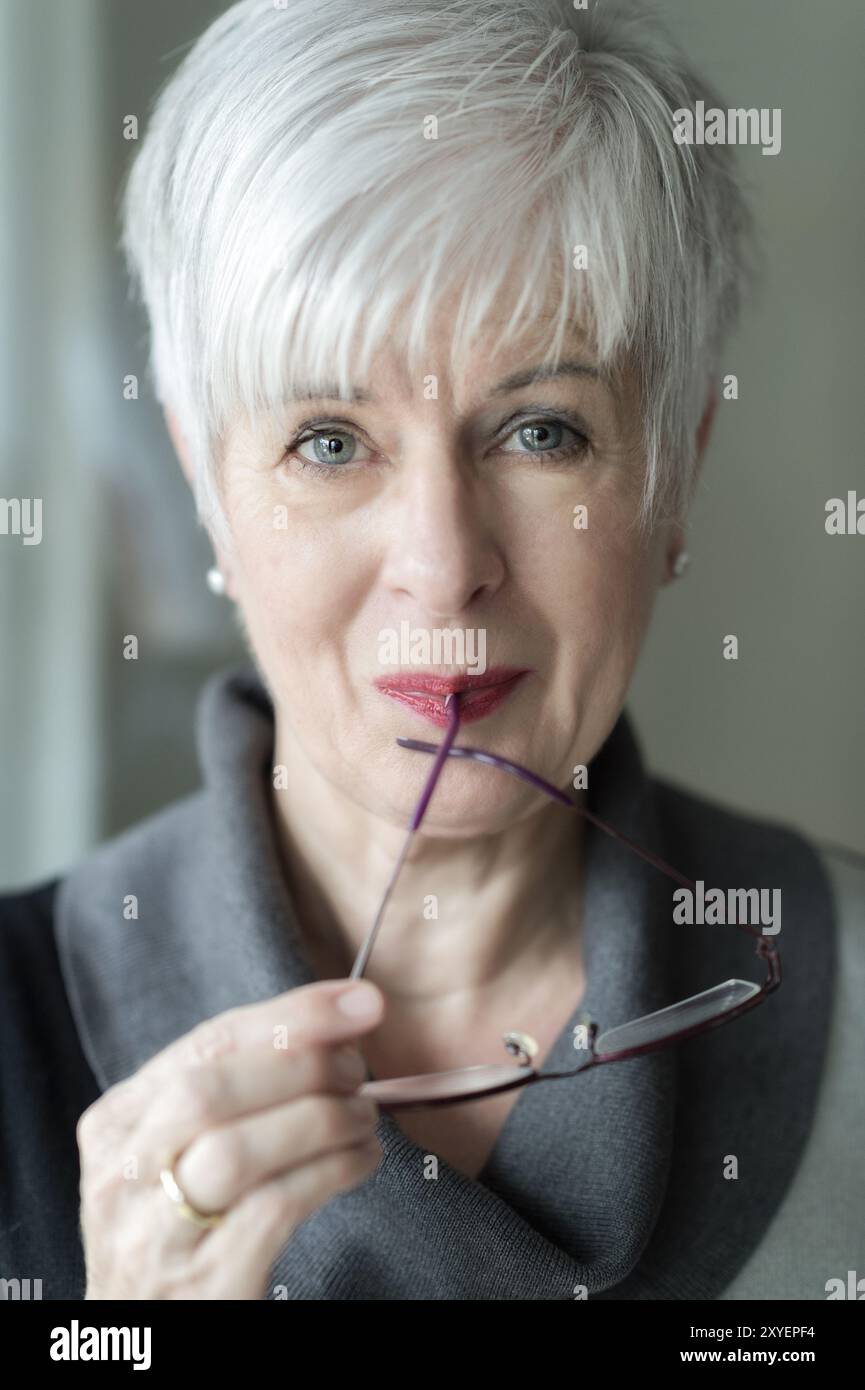 A good-looking older lady with grey hair and a camera look holds the ...
