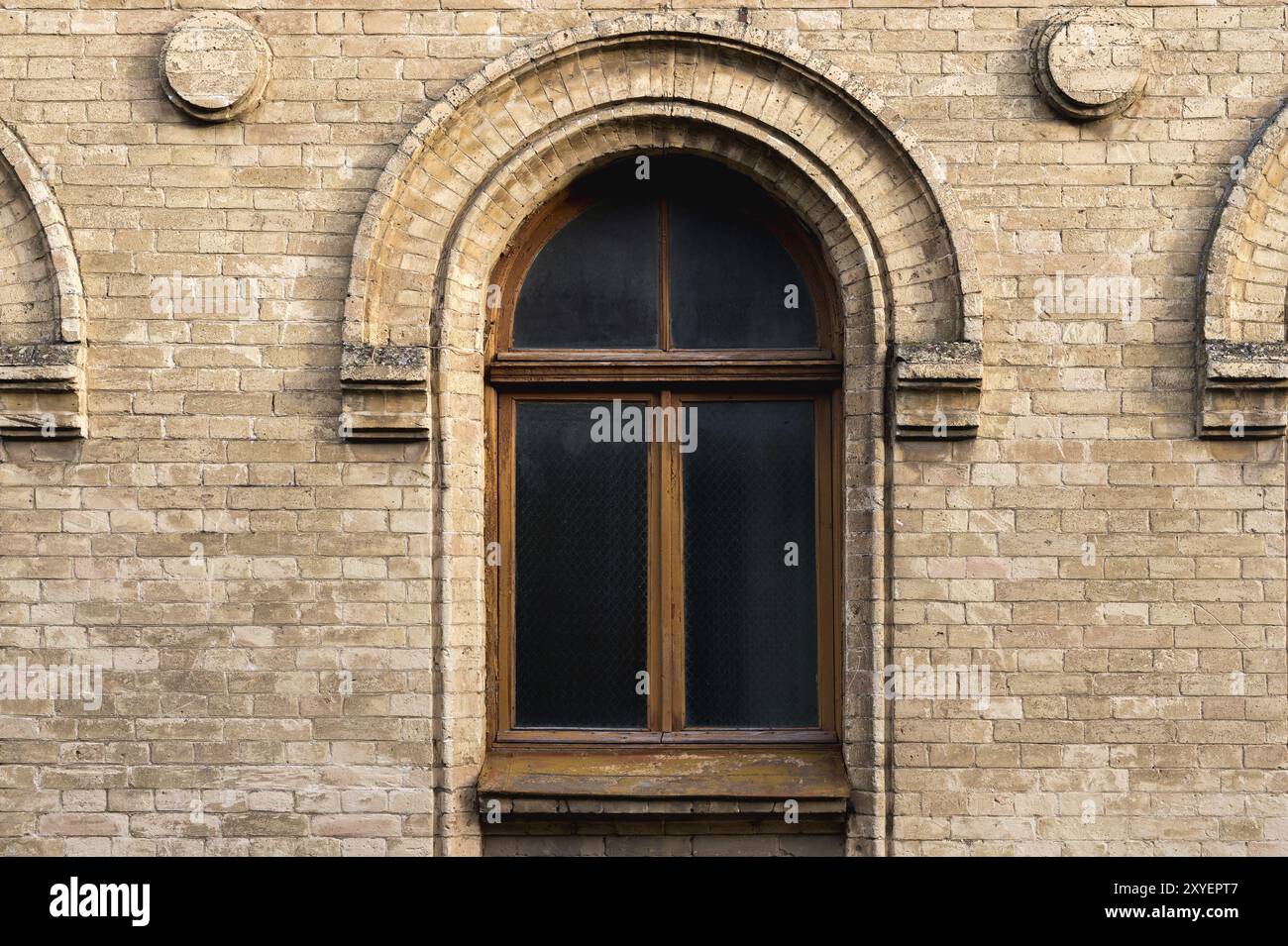 Vintage arched window in the wall of yellow brick. Black glass in a ...