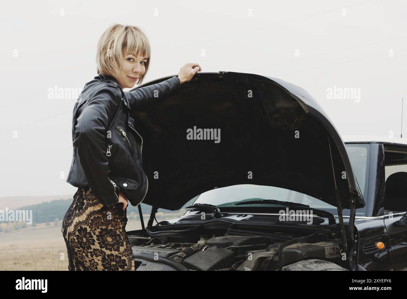 The blond girl opens the hood of her car and looks at the engine ...
