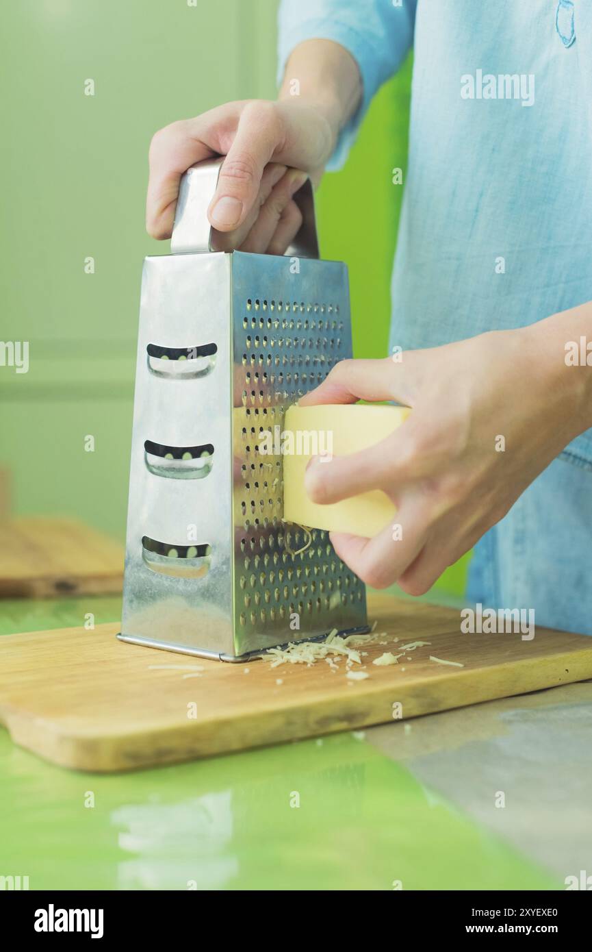 Close-up of a woman's hands rub a parmesan cheese on a metal grater on ...