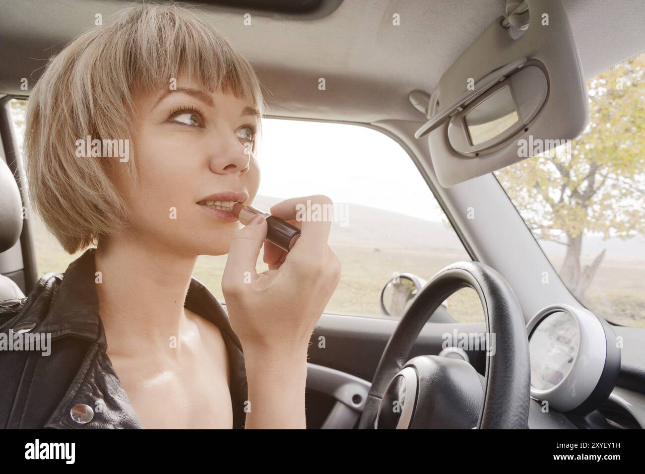 Cute blond woman with short hair coloring lips while sitting at the ...