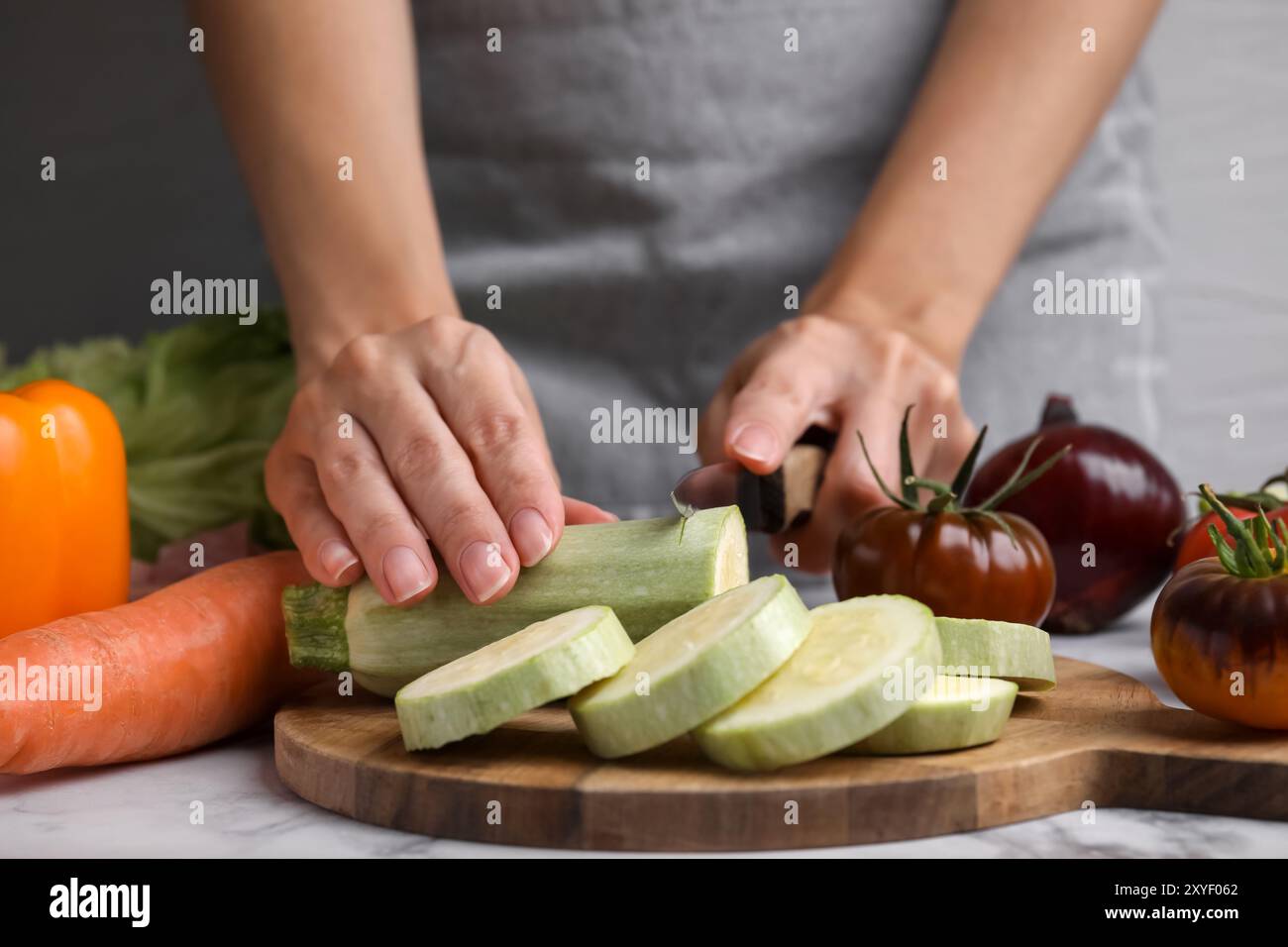 Cooking vegetable stew. Woman cutting zucchini at white marble table ...