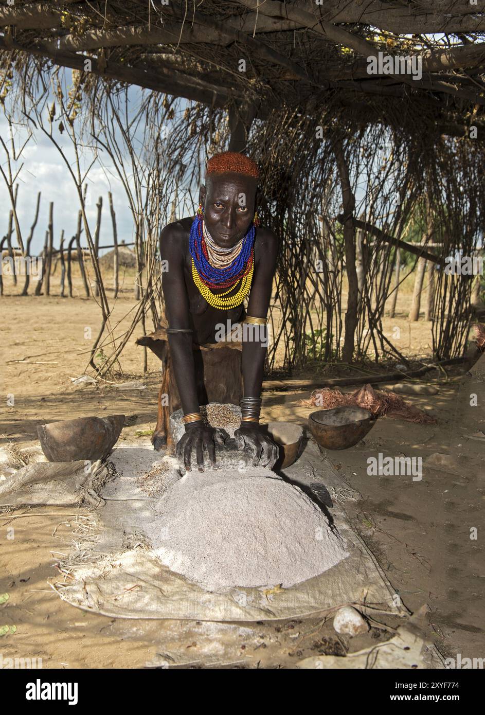 Woman from the Arbore ethnic group grinding red sorghum millet on a ...
