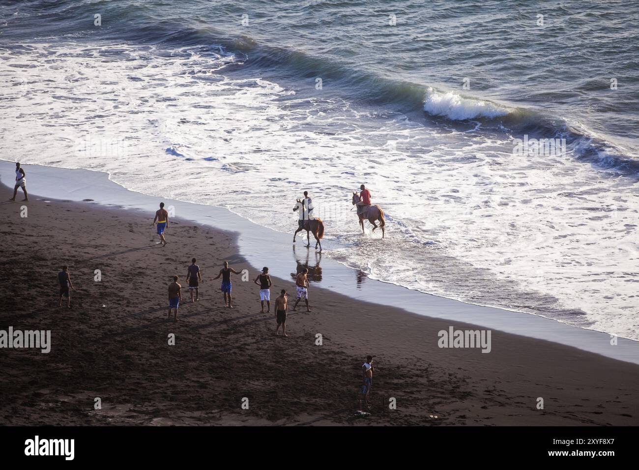 Two riders on horses ride along a beach, past people bathing Stock ...