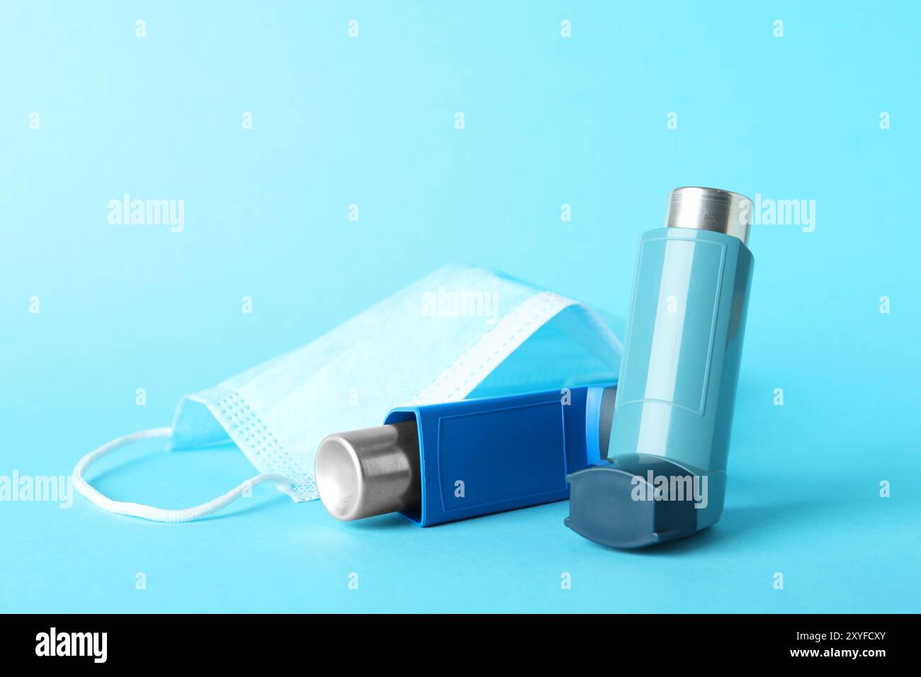 Asthma inhalers and medical mask on light blue background, closeup ...
