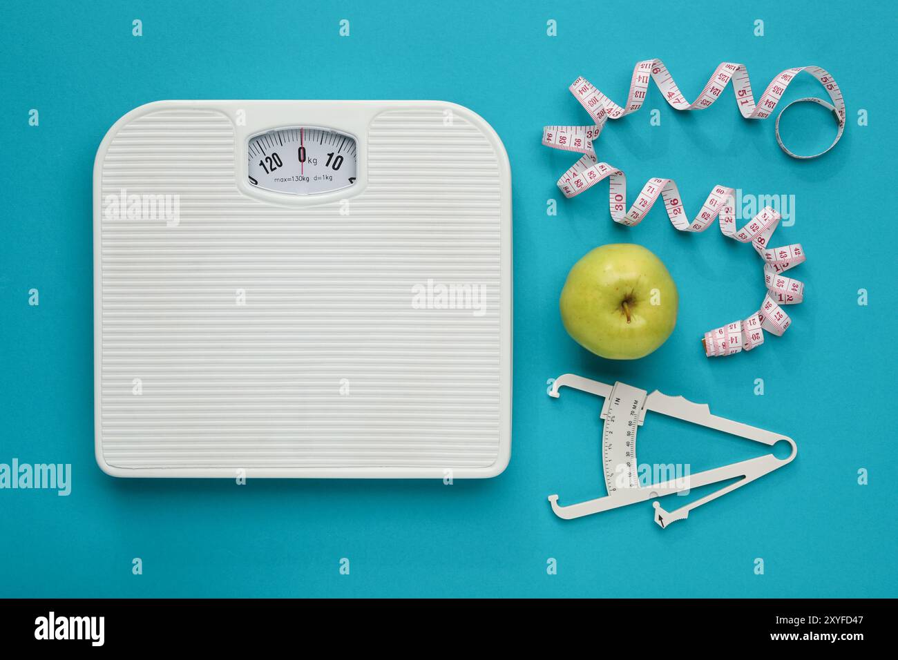 Body fat caliper, measuring tape, scale and apple on light blue ...