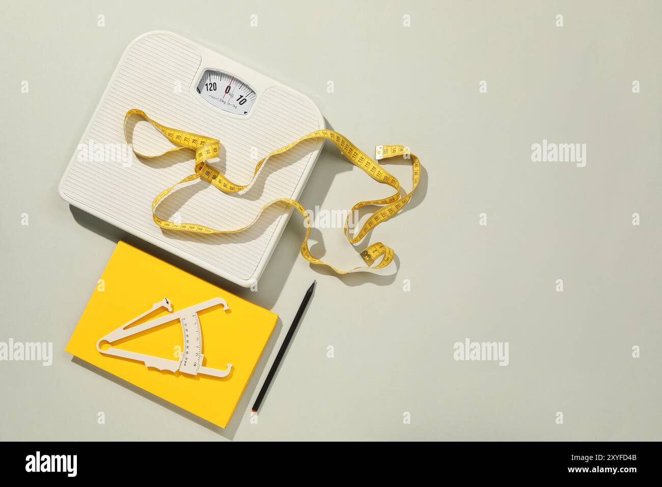 Body fat caliper, measuring tape, scale and notebook on light grey ...