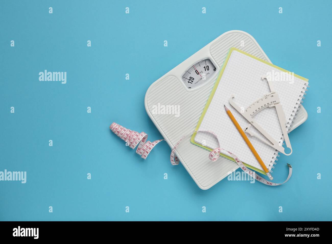 Body fat caliper, measuring tape, scale and notebook on light blue ...