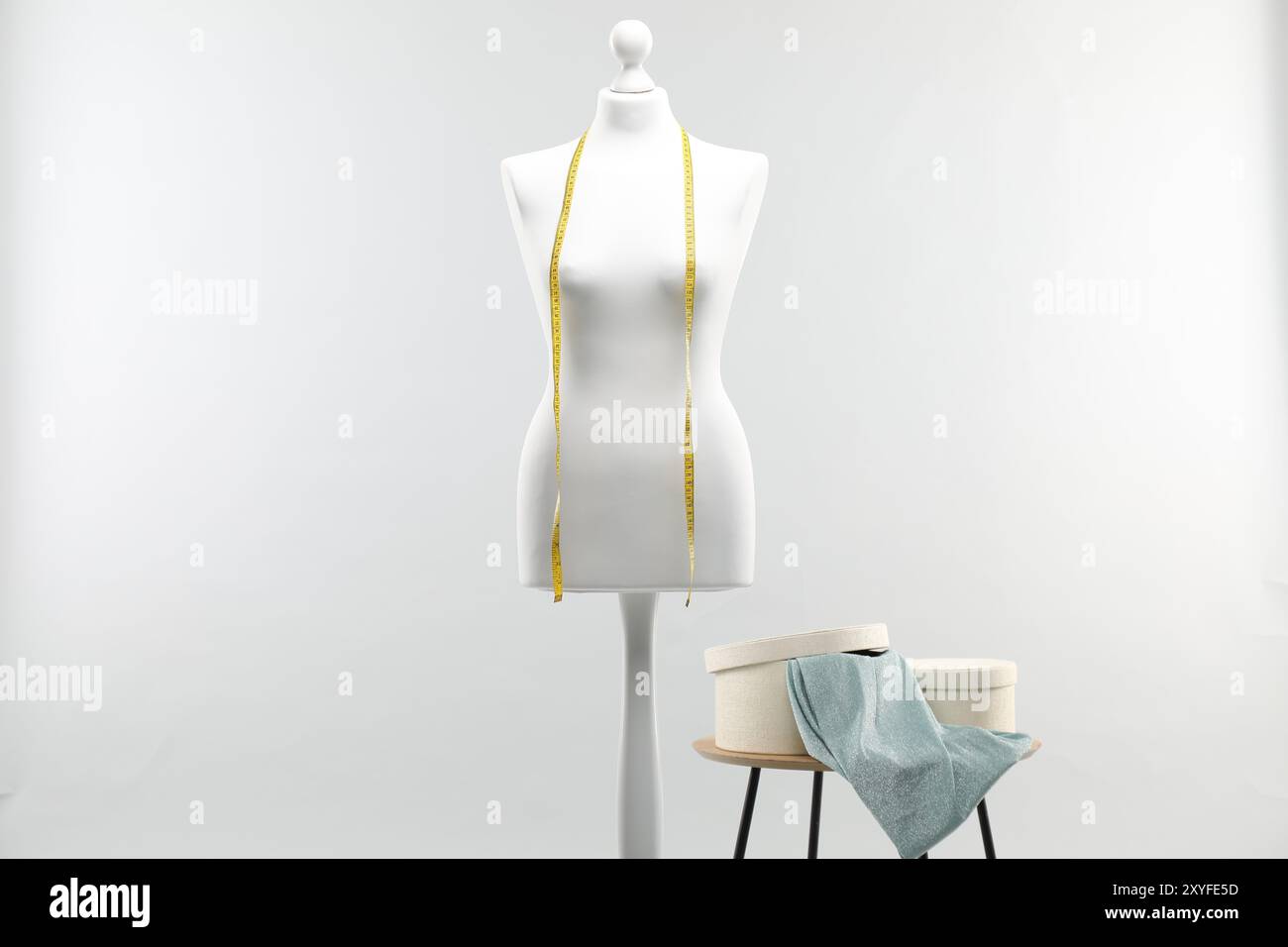 Mannequin with measuring tape and fabric in boxes on side table against ...