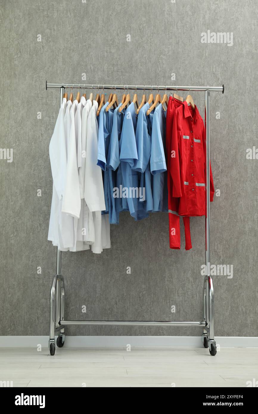 Different medical workers' uniforms on clothing rack against grey ...