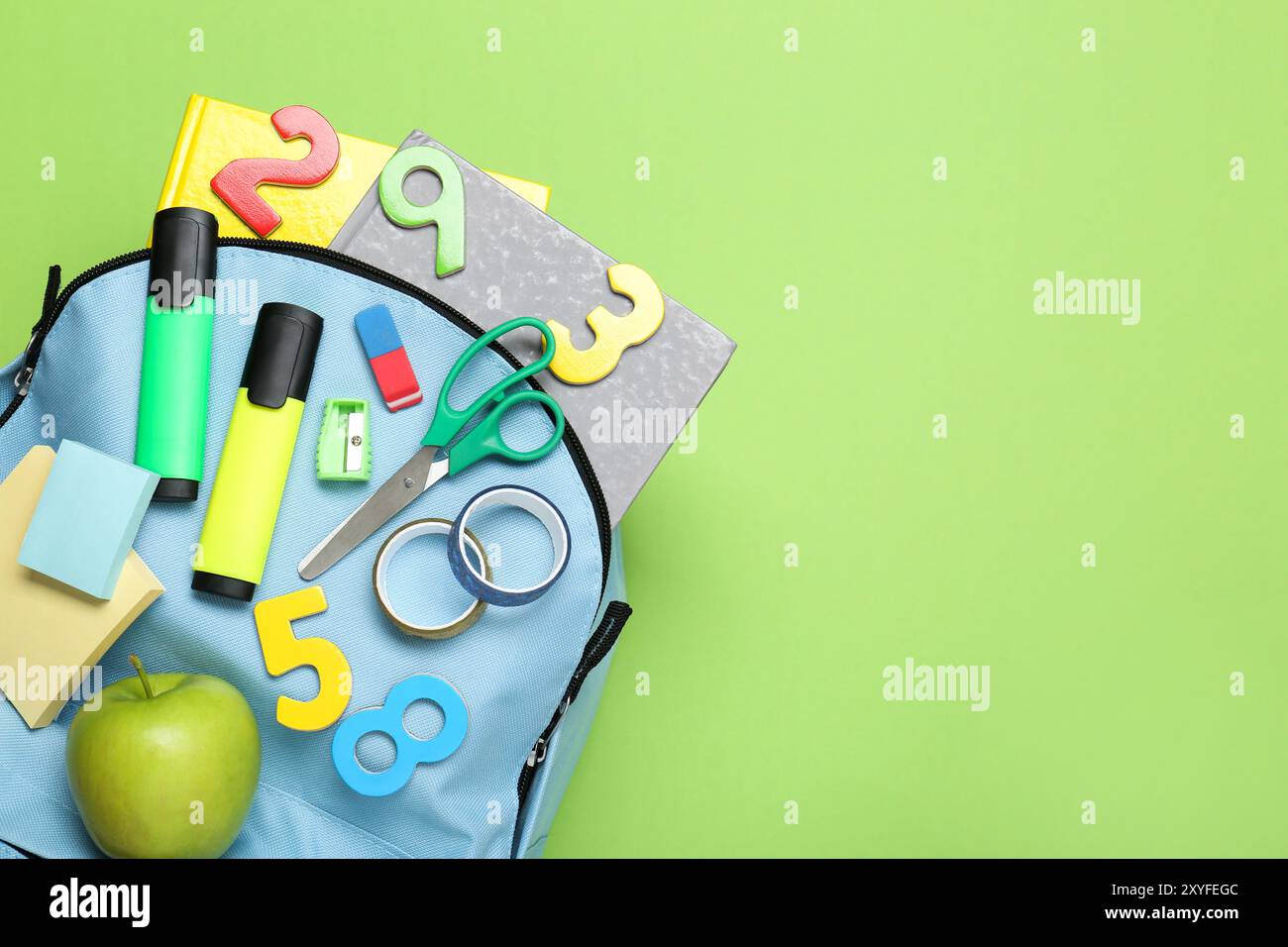 Light blue school backpack with stationery on green background, top ...
