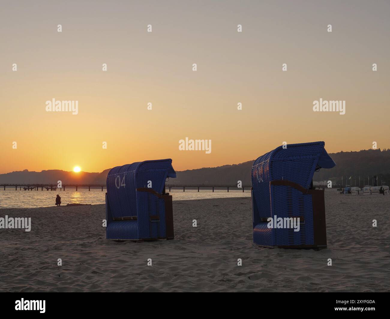 Two blue beach chairs on the beach at sunset, pier in the background ...