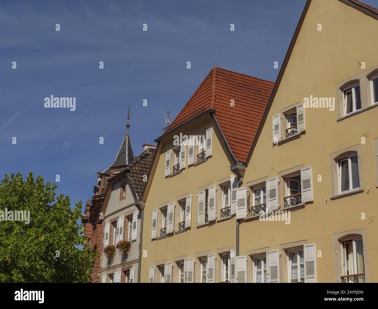 Row of light-coloured houses with shutters and red roofs under a bright ...