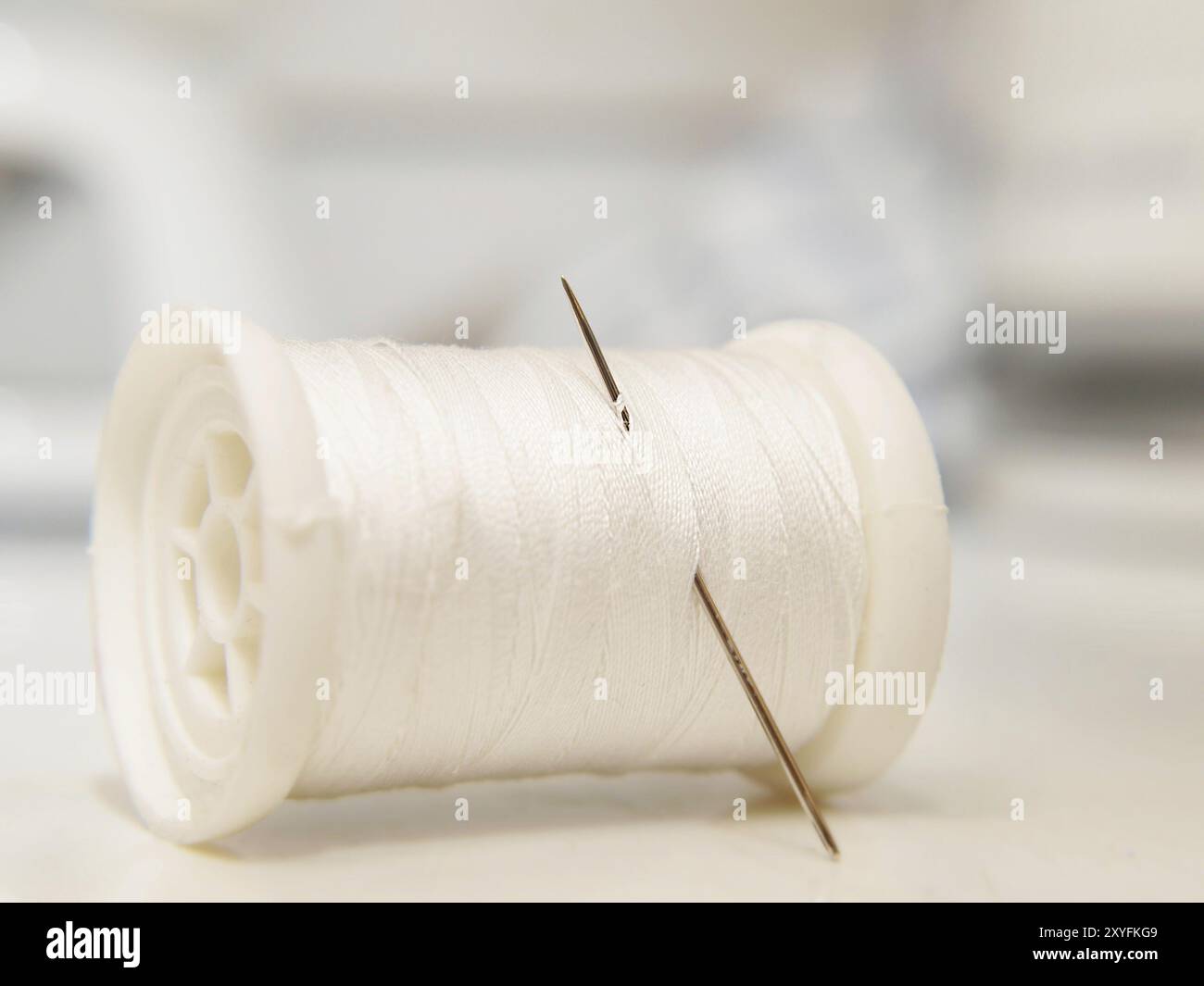 White thread on spool, laying down, with a needle Stock Photo - Alamy